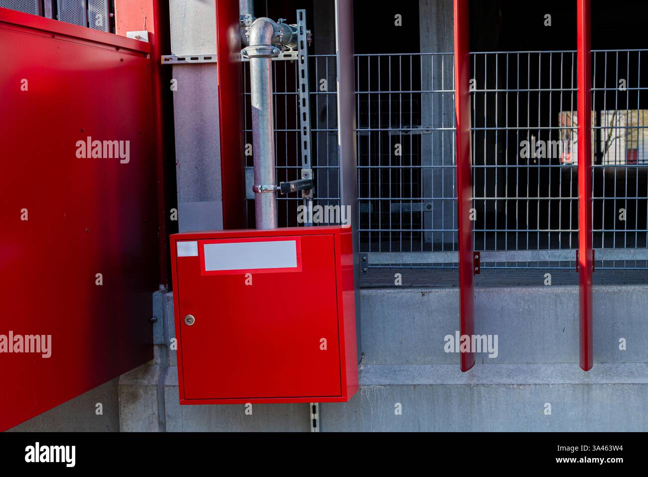 A red fire alarm box is securely mounted on a concrete wall next to a ...