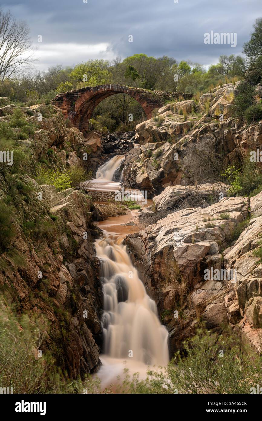 A historic stone bridge with an elegant arch spans over a small ...