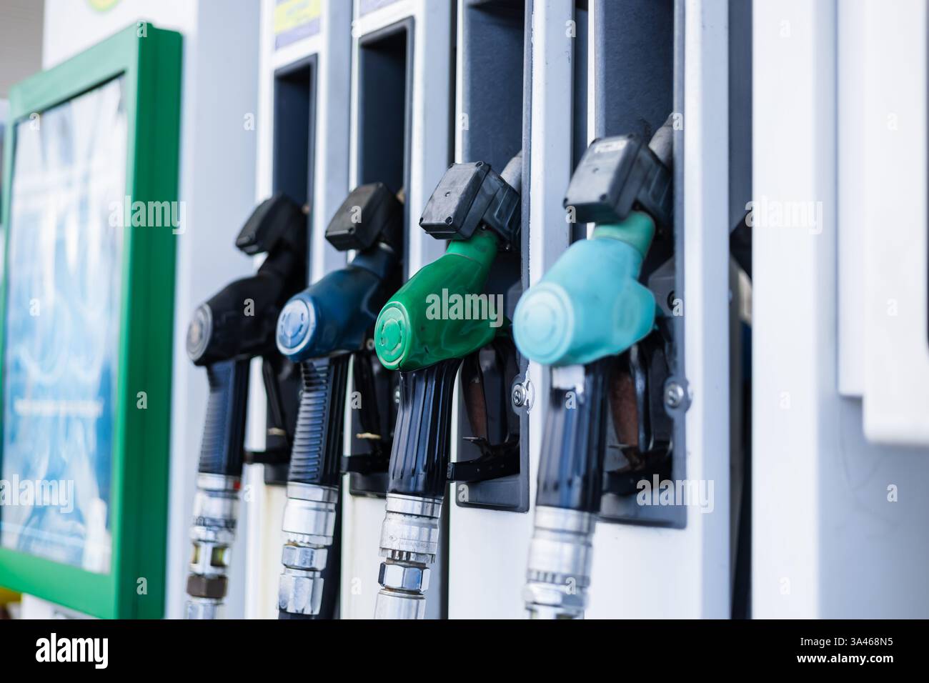 Four fuel pumps stand in a row at a gas station, each with different colored nozzles indicating ...