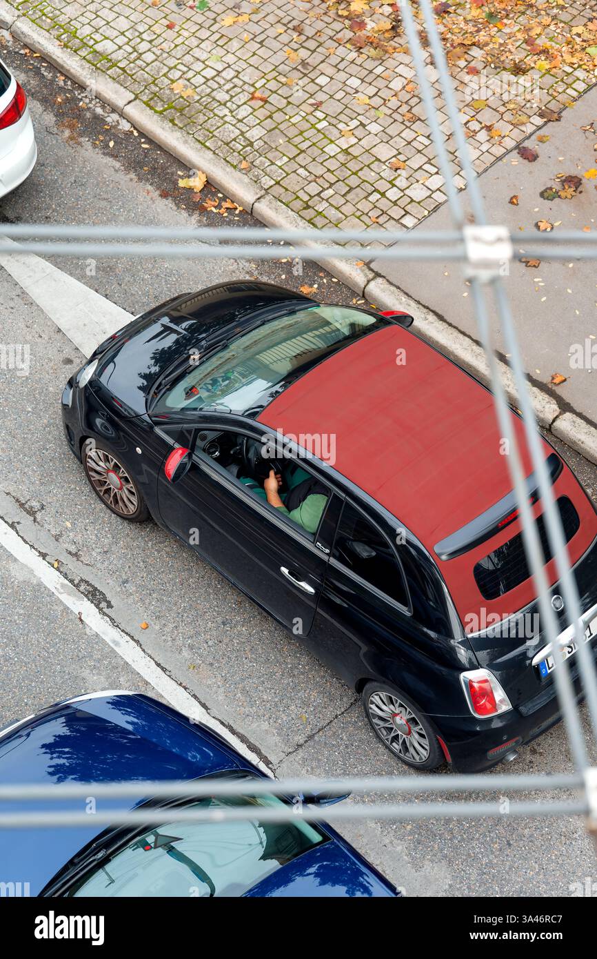 A black car with a bright red convertible roof, stopped at a traffic ...