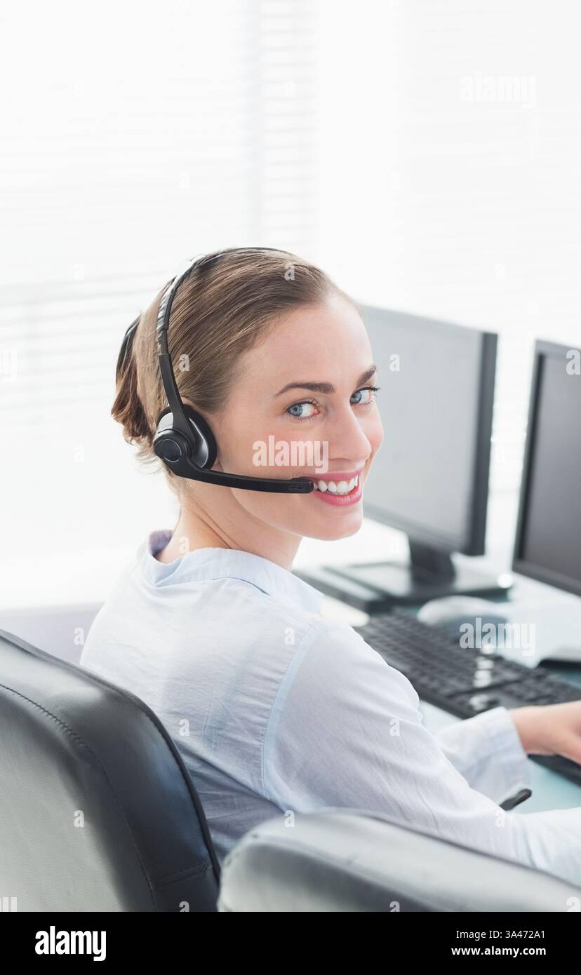 Customer service representative wearing headset smiling at desk in ...