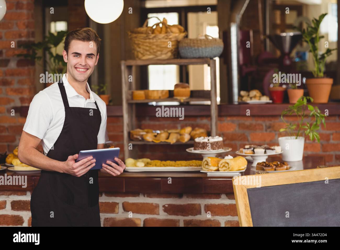 Barista holding tablet smiling in bakery with fresh pastries and bread ...