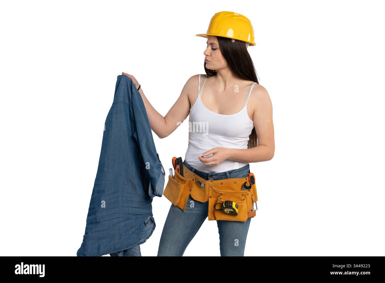 Young female construction worker wearing a yellow hard hat and tool belt, examining her denim ...