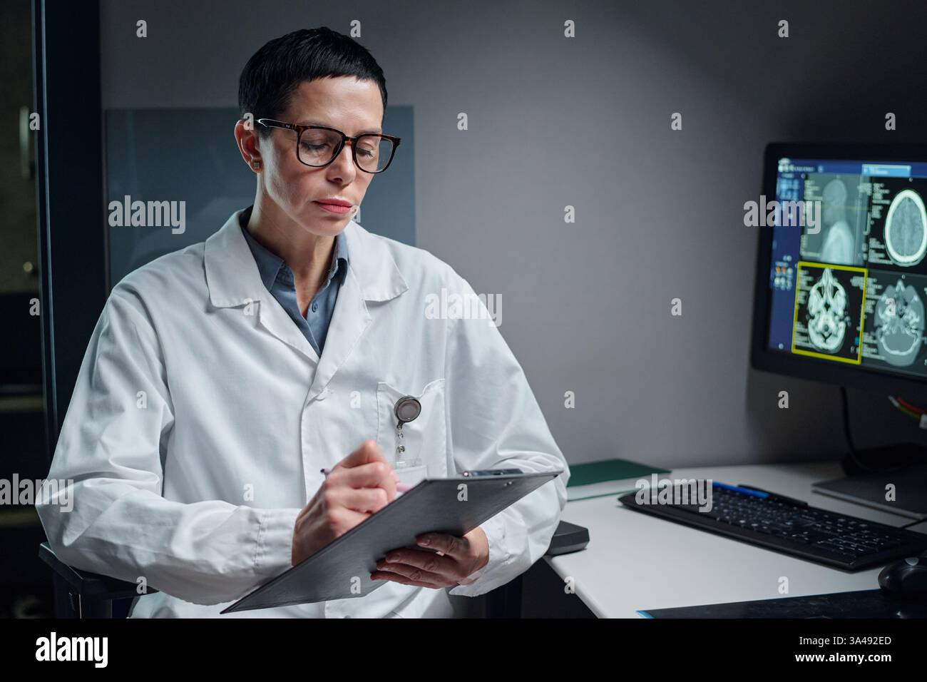 Female doctor wearing white coat, holding tablet, sitting at desk ...