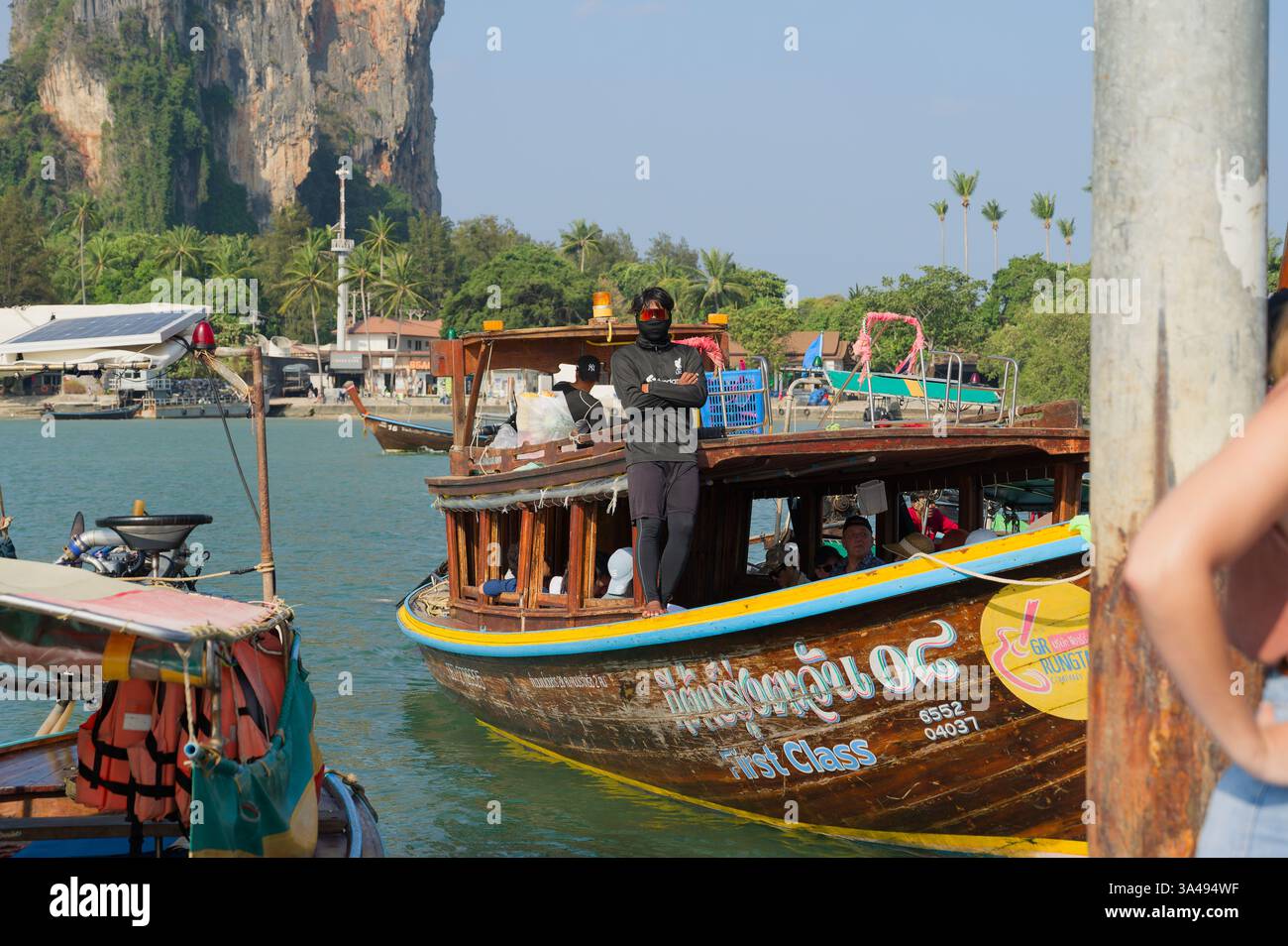 Boat worker stands confidently on a traditional wooden long-tail boat ...