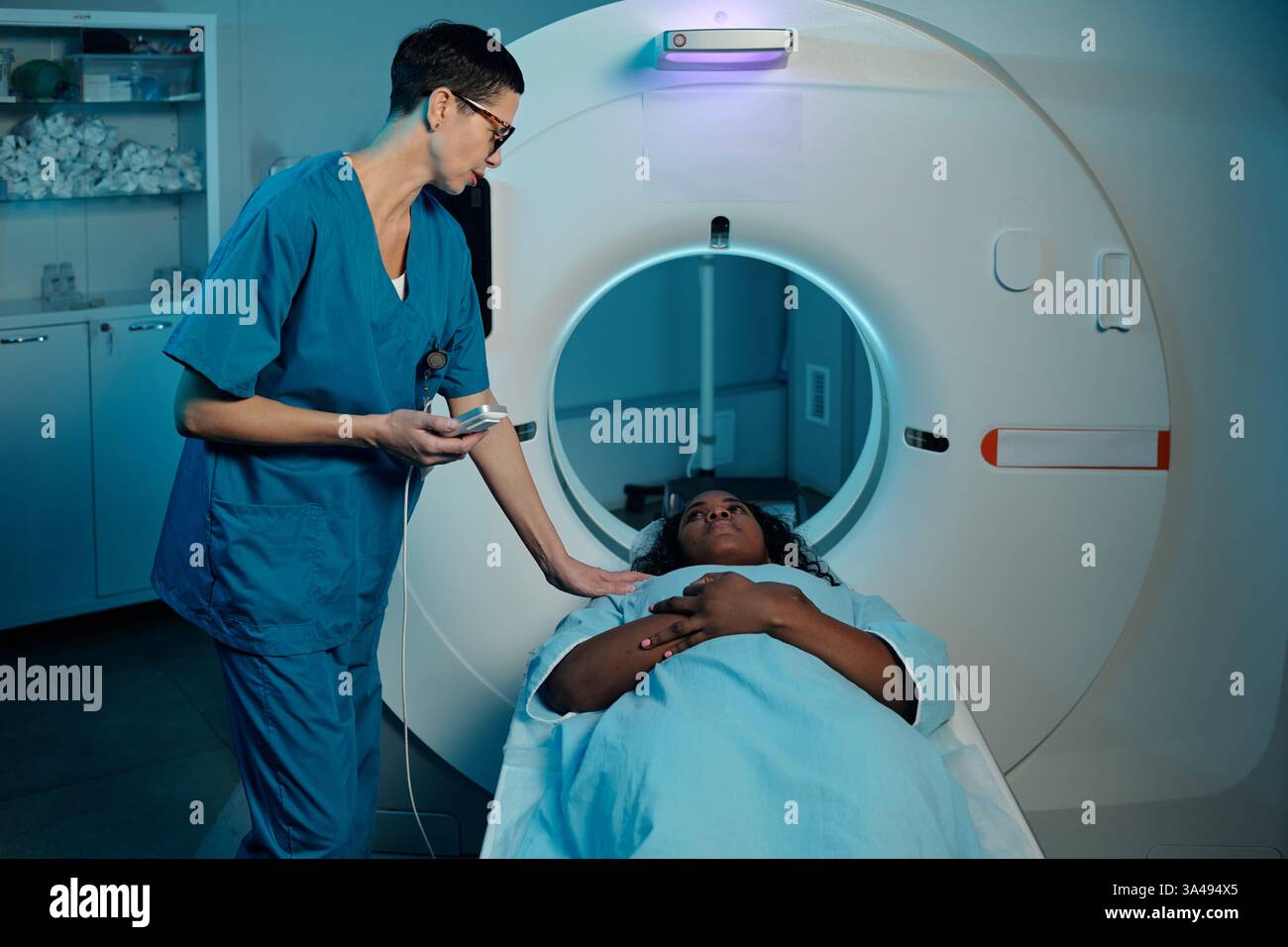 Medical professional preparing patient for MRI scan in medical facility. Patient lying down on ...