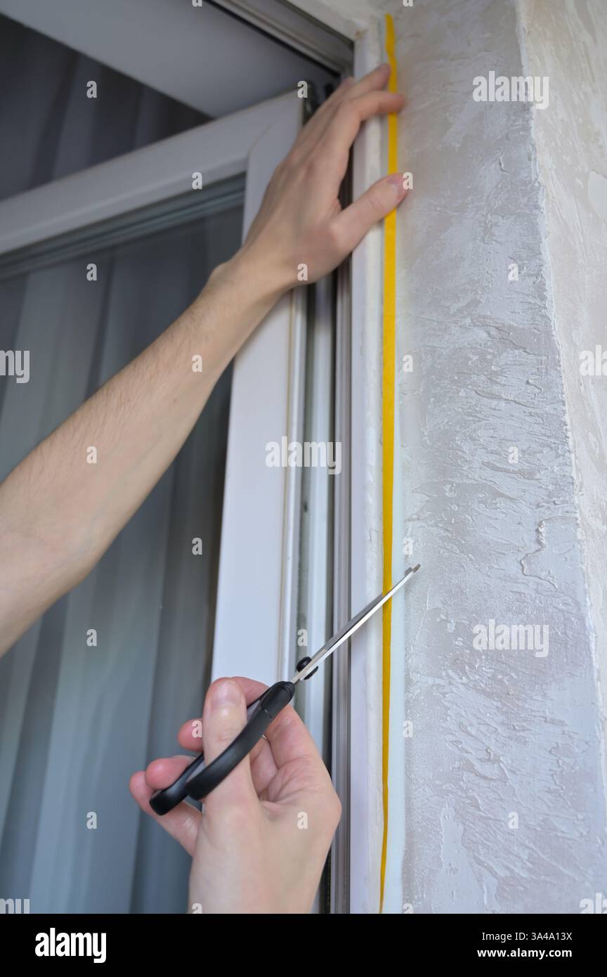 A man cuts the foam adhesive tape with scissors. Insulates windows and ...