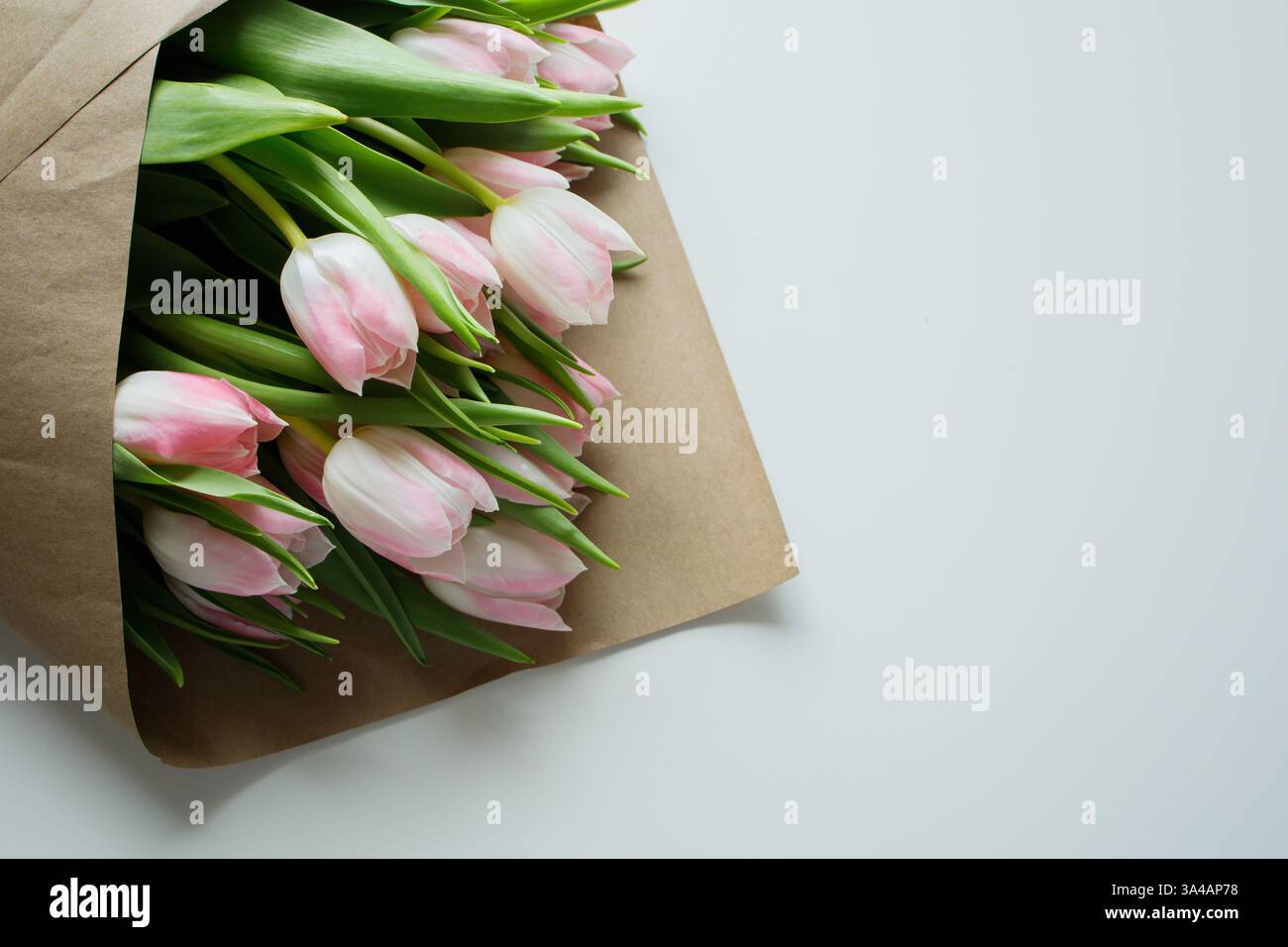 Pink tulips bouquet wrapped in brown craft paper on white background ...