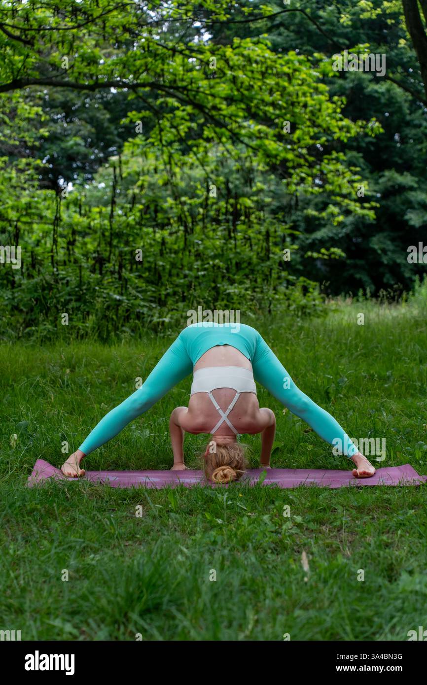 Flexible woman practicing wide-legged forward fold yoga pose on mat in ...