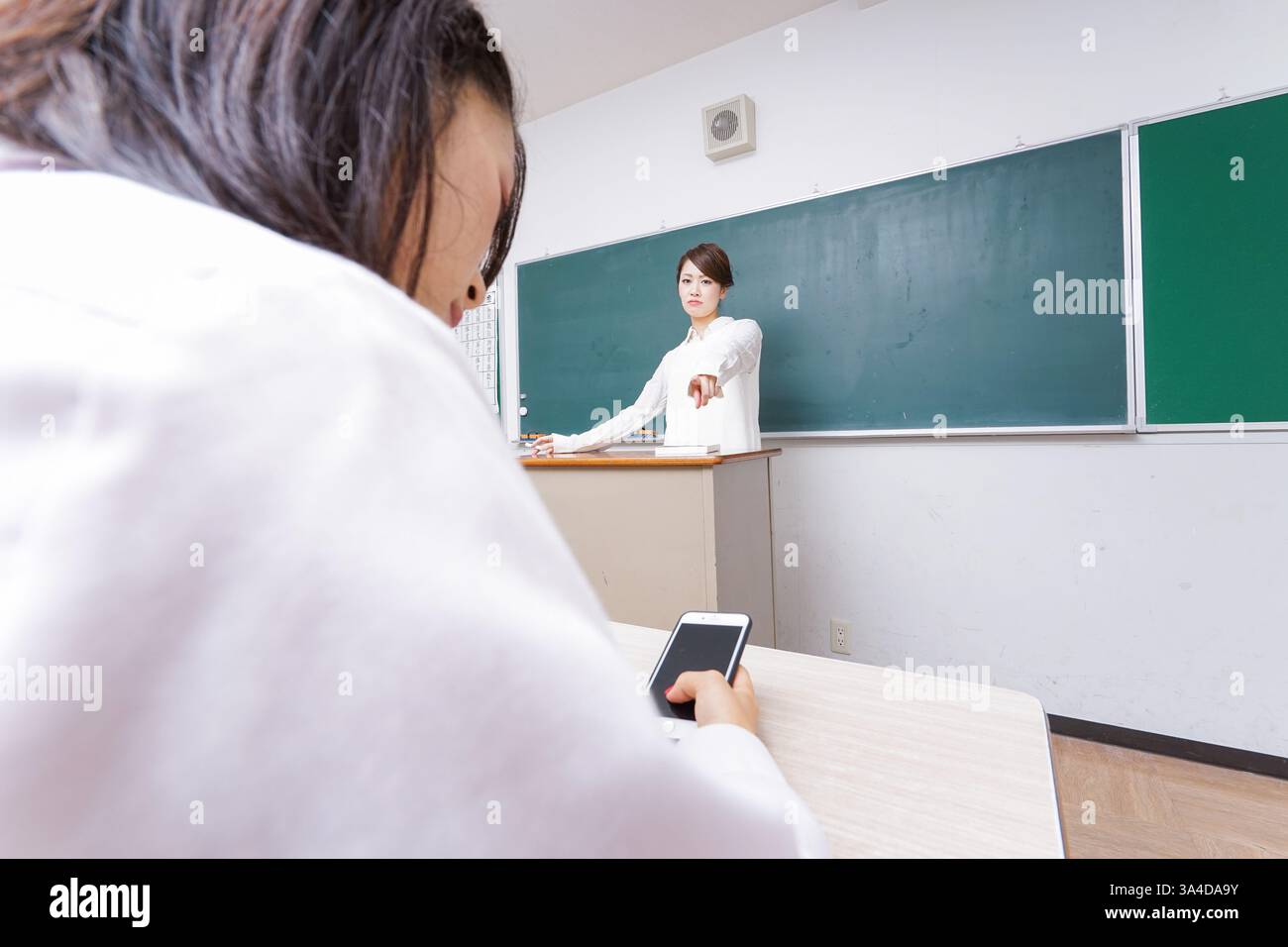 Student using a smartphone during class and teacher cautioning her ...