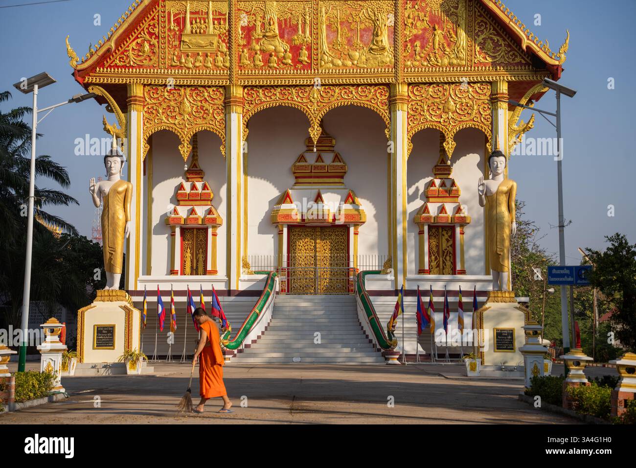 A monk sweeping the grounds of a beautiful temple in Laos, showcasing ...