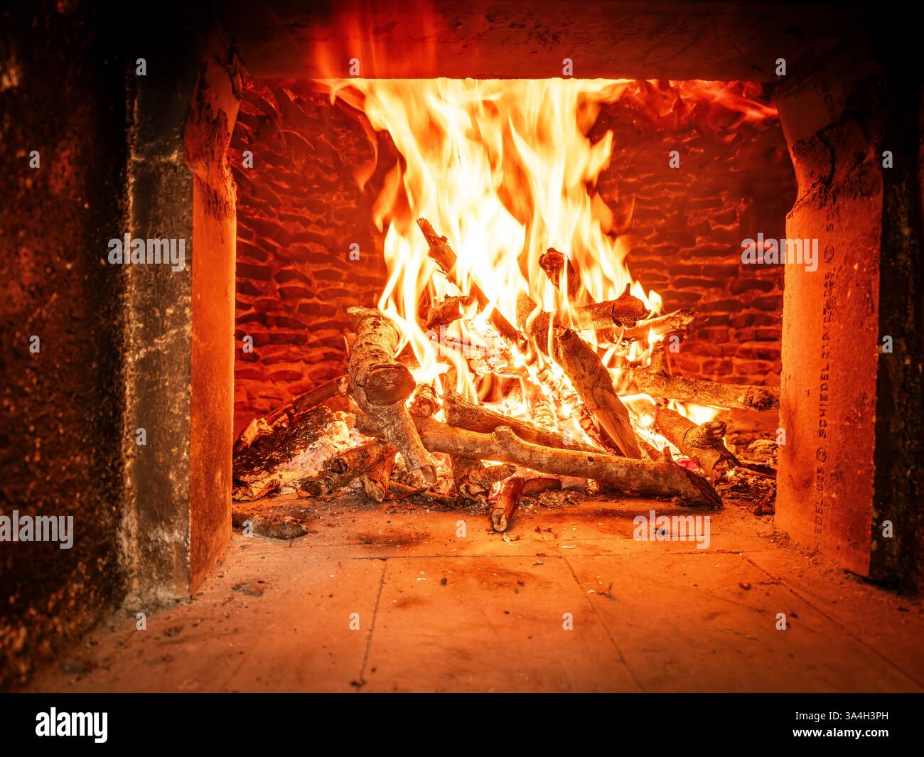 A roaring fire with glowing logs burns inside a rustic brick fireplace ...