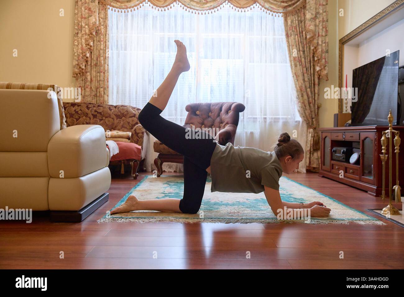 Woman practicing yoga on a rug at home, performing a raised leg pose ...