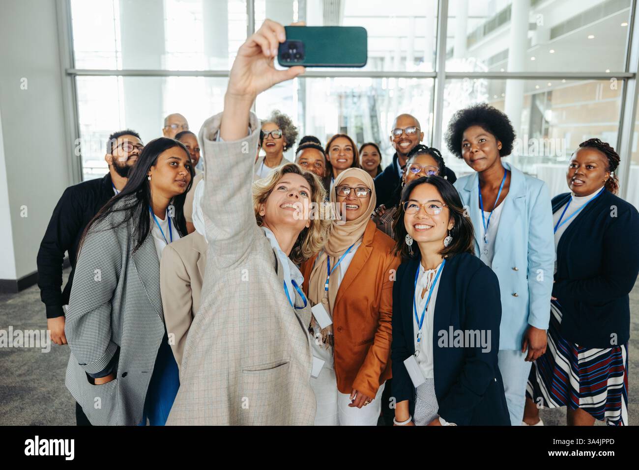 A diverse business team gathers for a group selfie at a company event, showcasing teamwork and ...