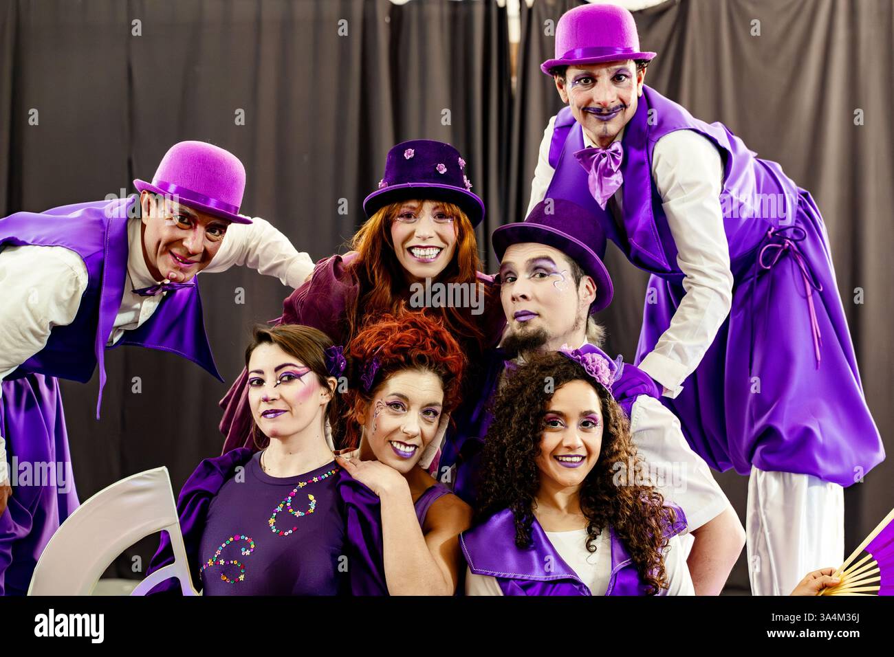 Group of smiling circus performers wearing purple costumes and stage ...