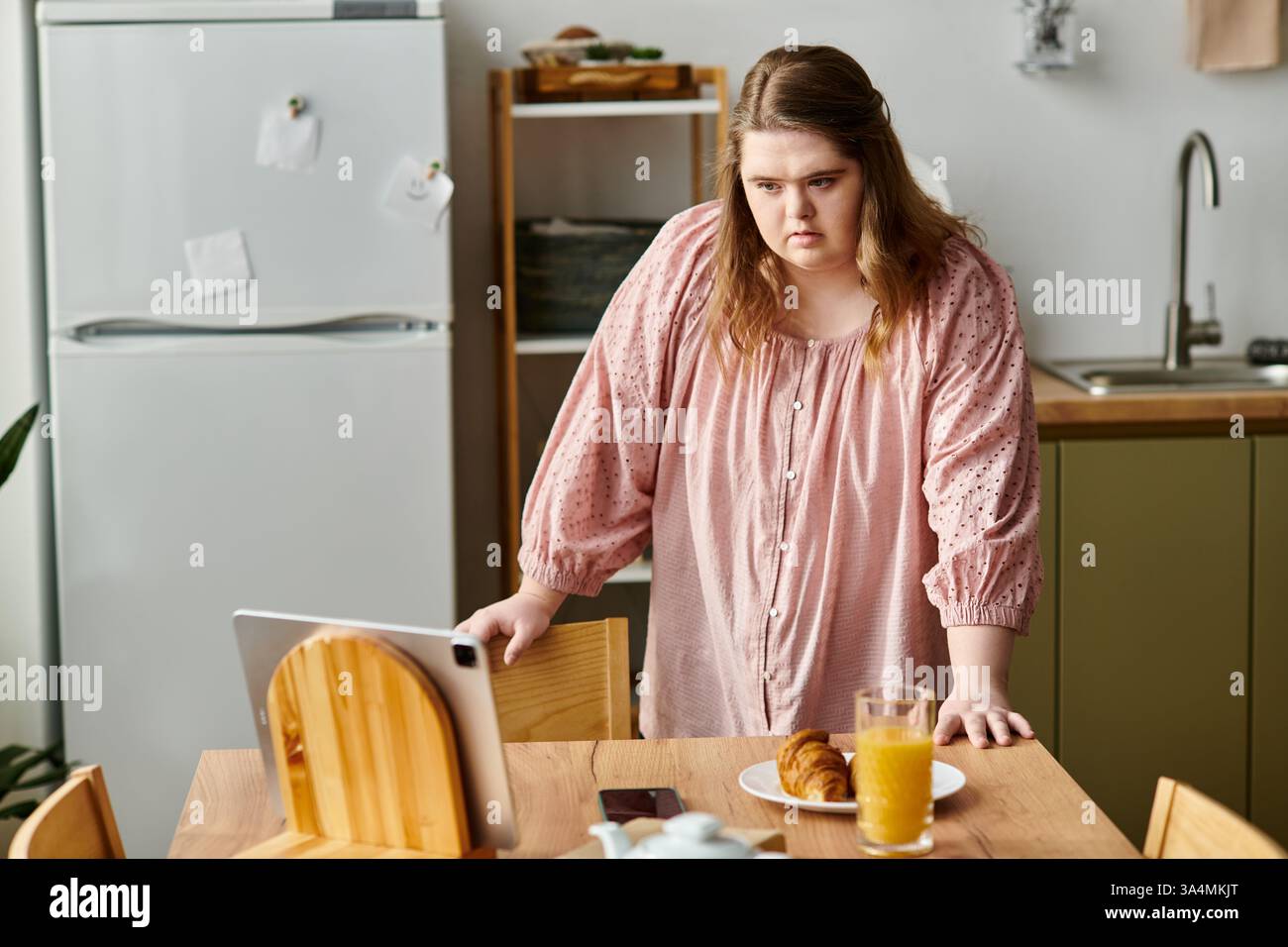 In a cozy kitchen, a young woman with Down syndrome enjoys breakfast ...