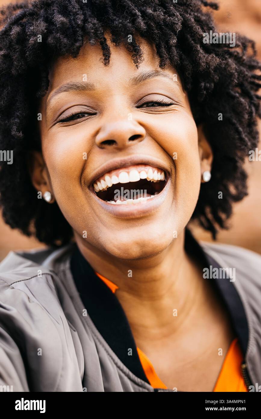Close-up portrait of a cheerful young woman with curly hair laughing ...