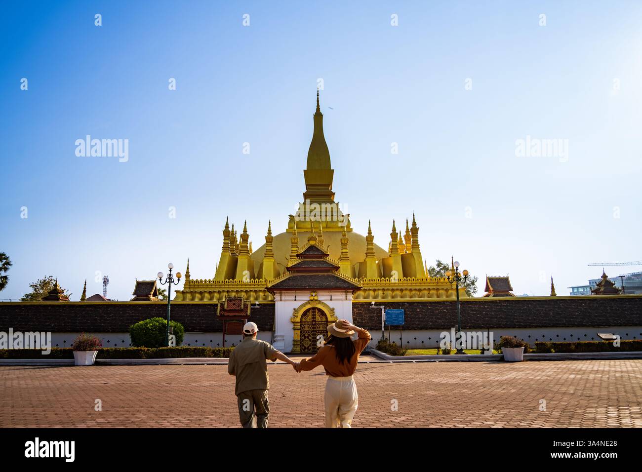 A couple walking towards the iconic Pha That Luang temple in Laos, capturing the beauty and ...