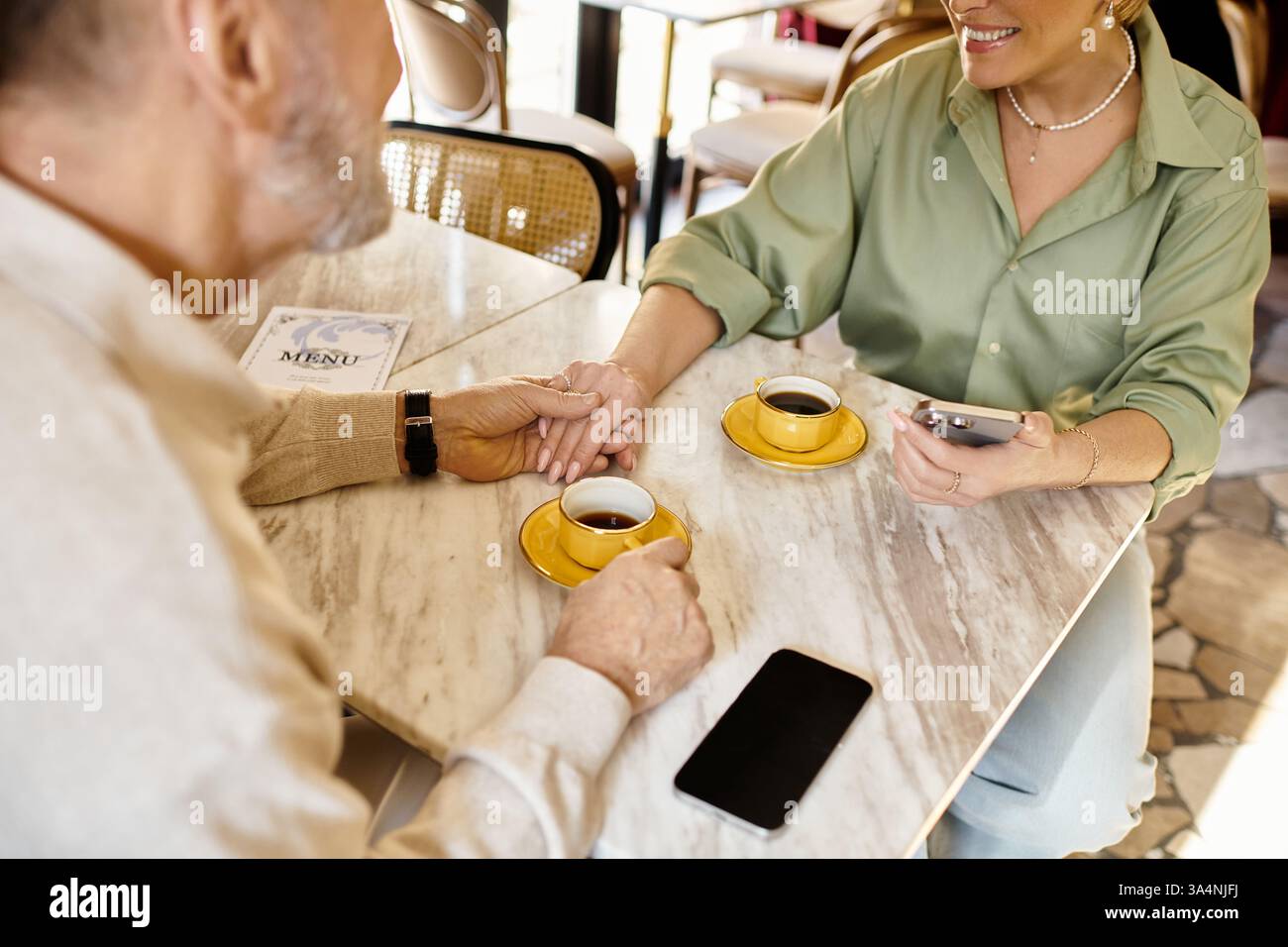 A mature couple shares a tender moment while sipping coffee and holding ...