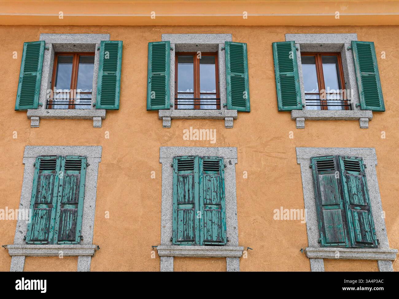 Facade of an old orange house with windows with green shutters closed ...