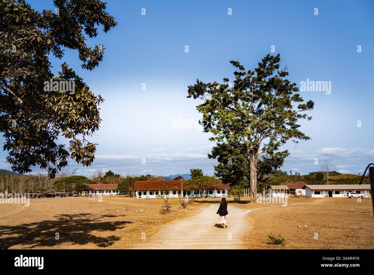 A woman walks along a dusty path towards a rural school under a vast ...