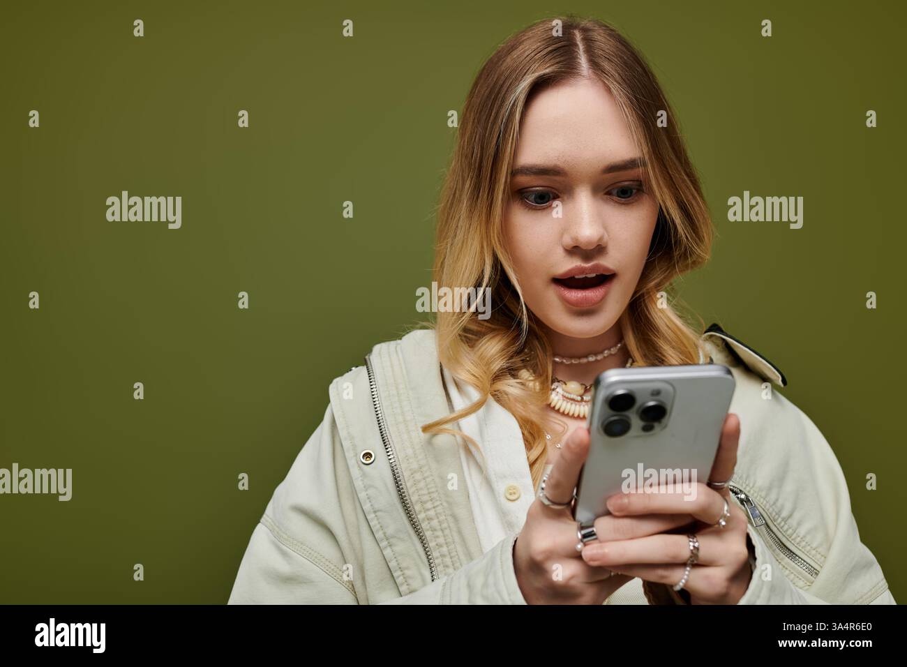 Stylish young woman expresses surprise while checking her smartphone in vibrant spring setting ...