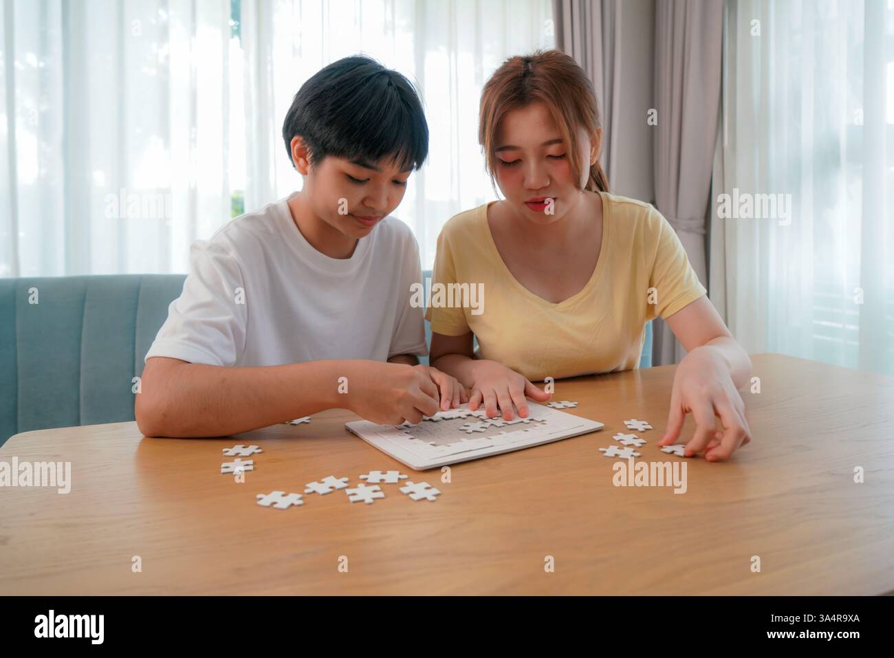 two asian friends working together on a puzzle at a wooden table ...