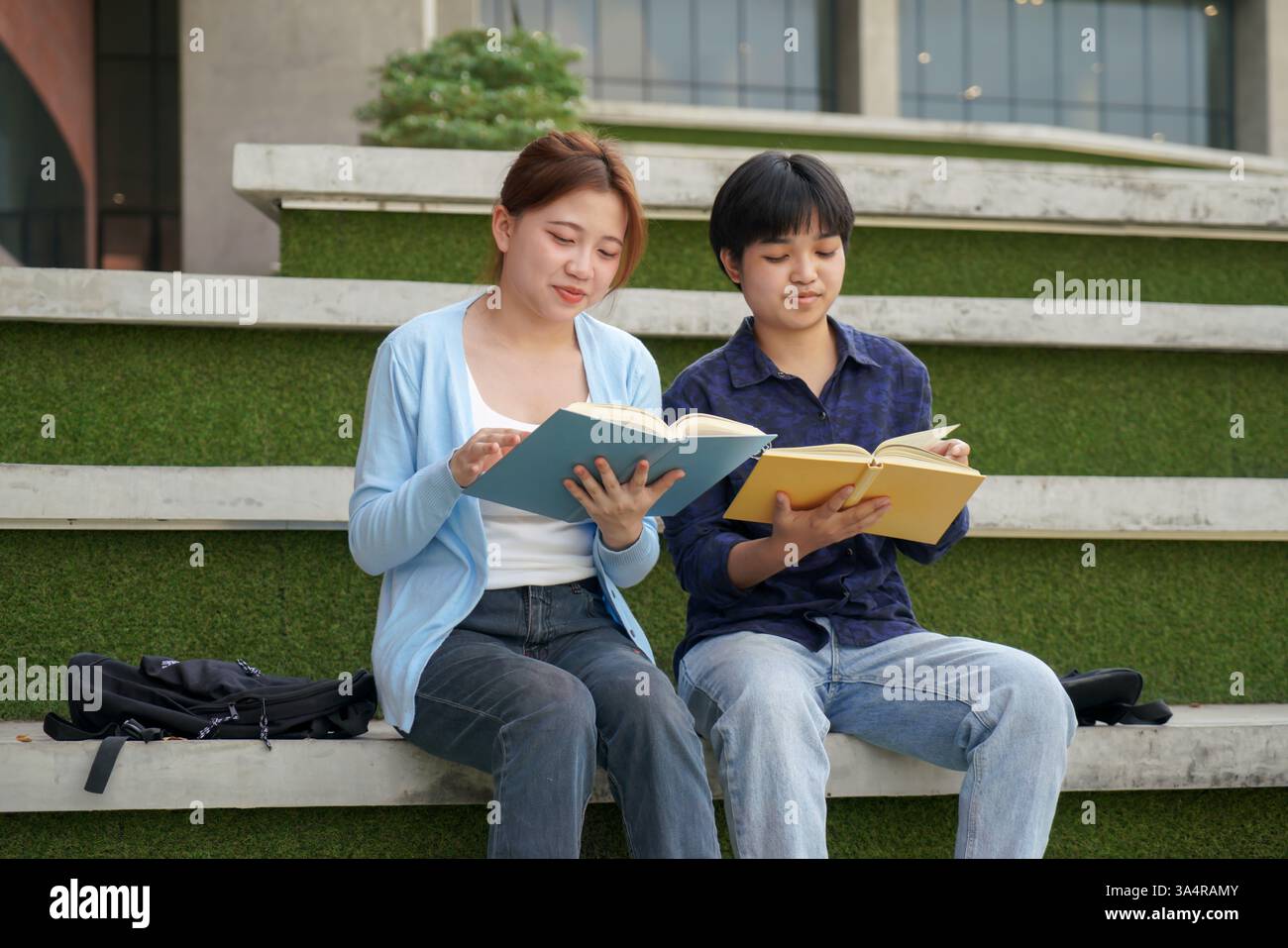 Relaxed scene of two asian college students seated on modern concrete ...