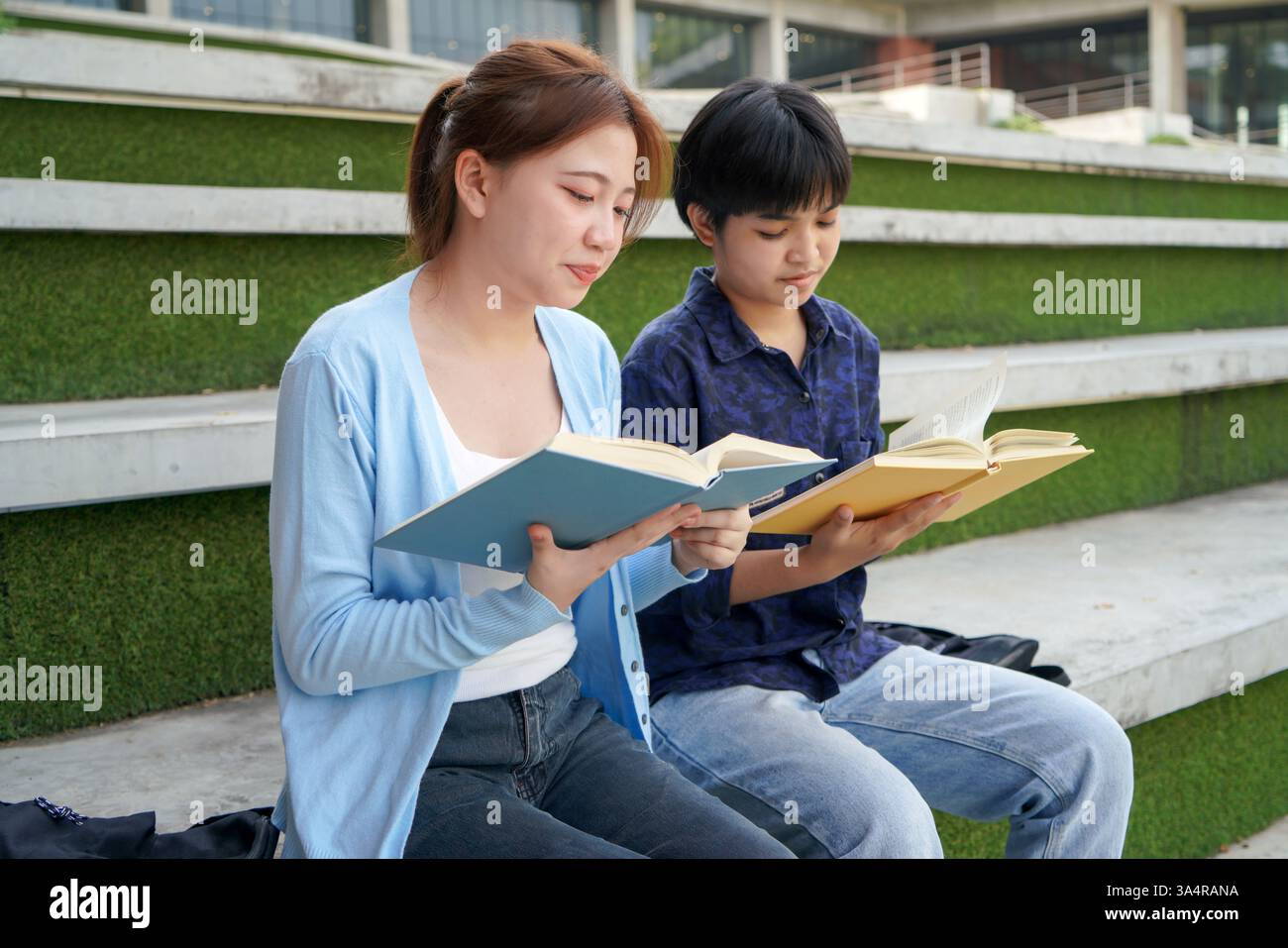 Relaxed scene of two asian college students seated on modern concrete ...