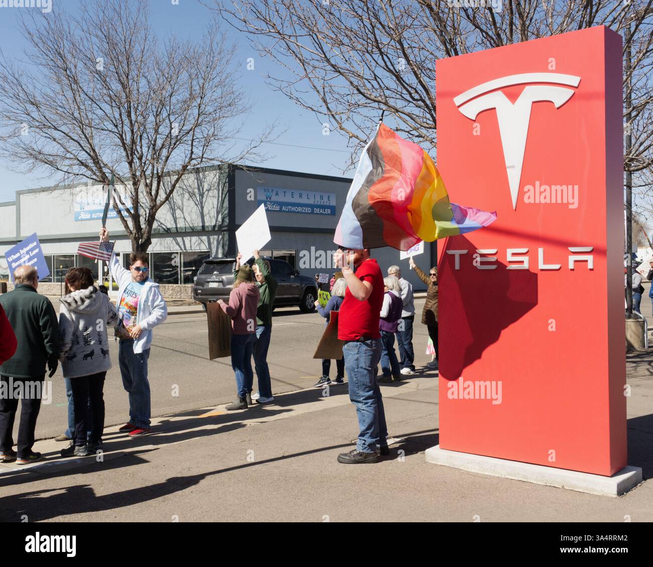 Lgbtq flag flown in front of a tesla sign with protestors lining the ...