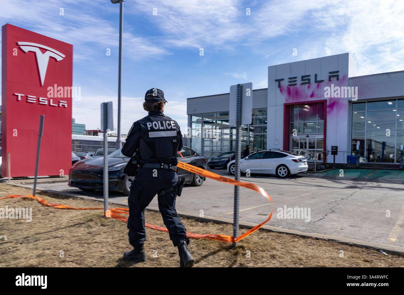 A police officer wraps up police tape from a Tesla dealership that was ...