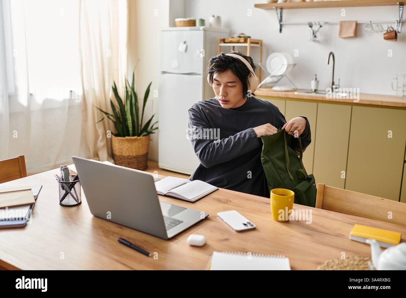 Student immersed in e-learning, unpacking his bag at a stylish home ...