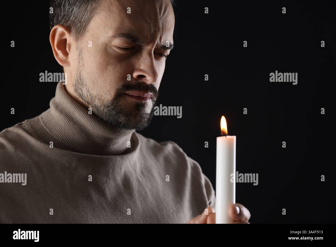 Sad man with burning candle crying on black background, space for text ...