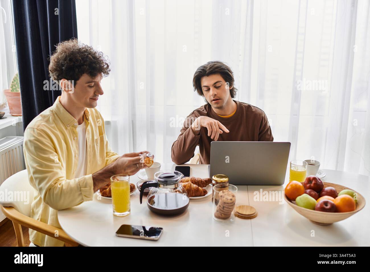 Two good-looking men share a cozy breakfast while working on a laptop ...