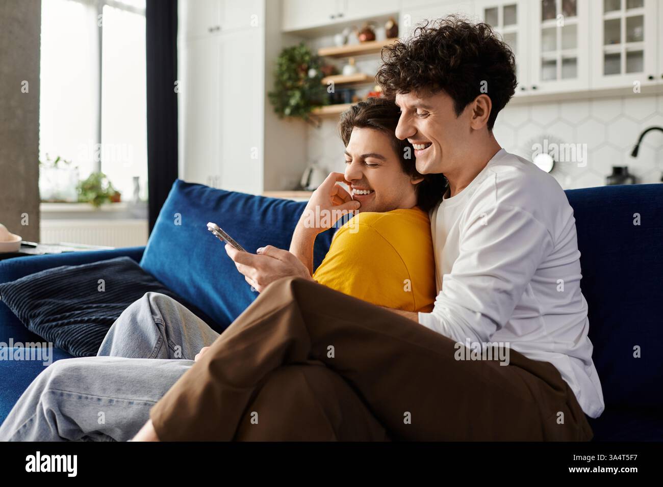 Two men cuddle closely on a couch while enjoying a moment of laughter ...