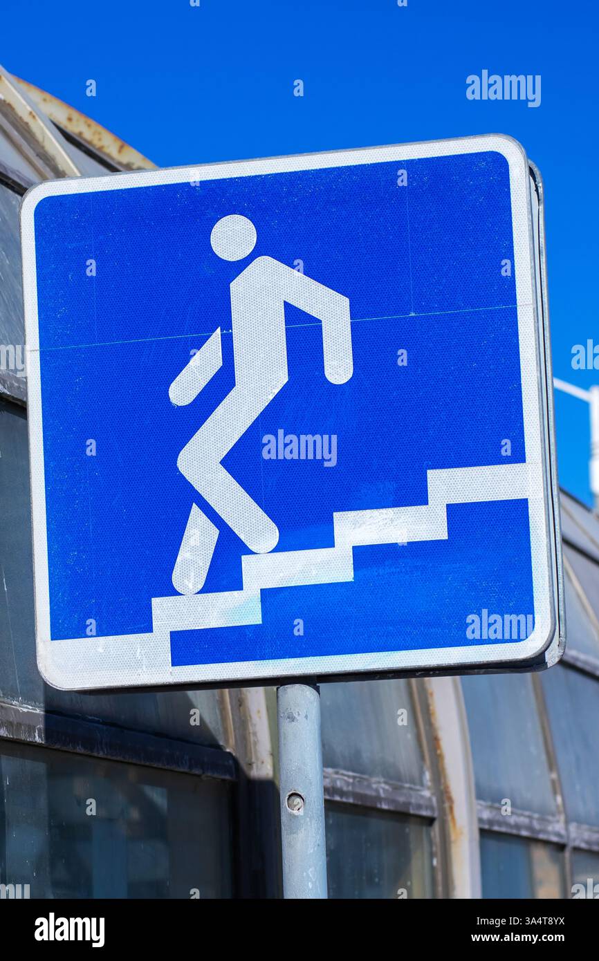 A vibrant blue sign depicts a figure ascending a set of stairs ...