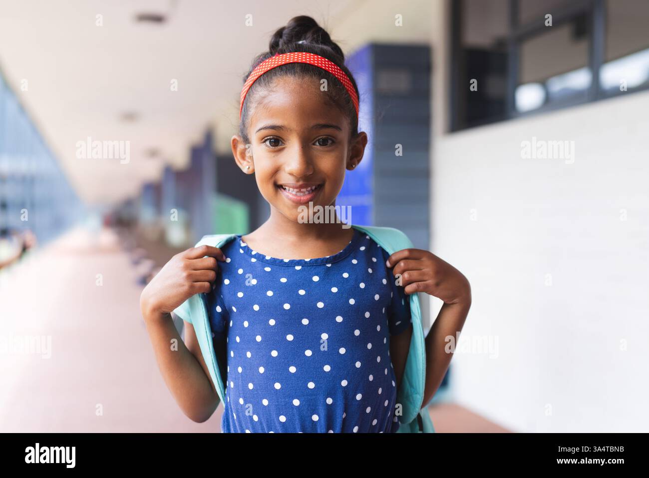 Smiling girl with backpack standing in school hallway, ready for class ...
