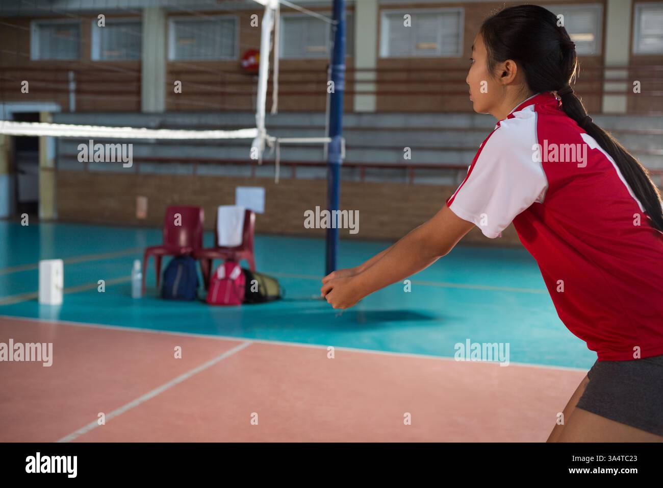 In school gym, girl in red jersey playing volleyball, focusing on game ...
