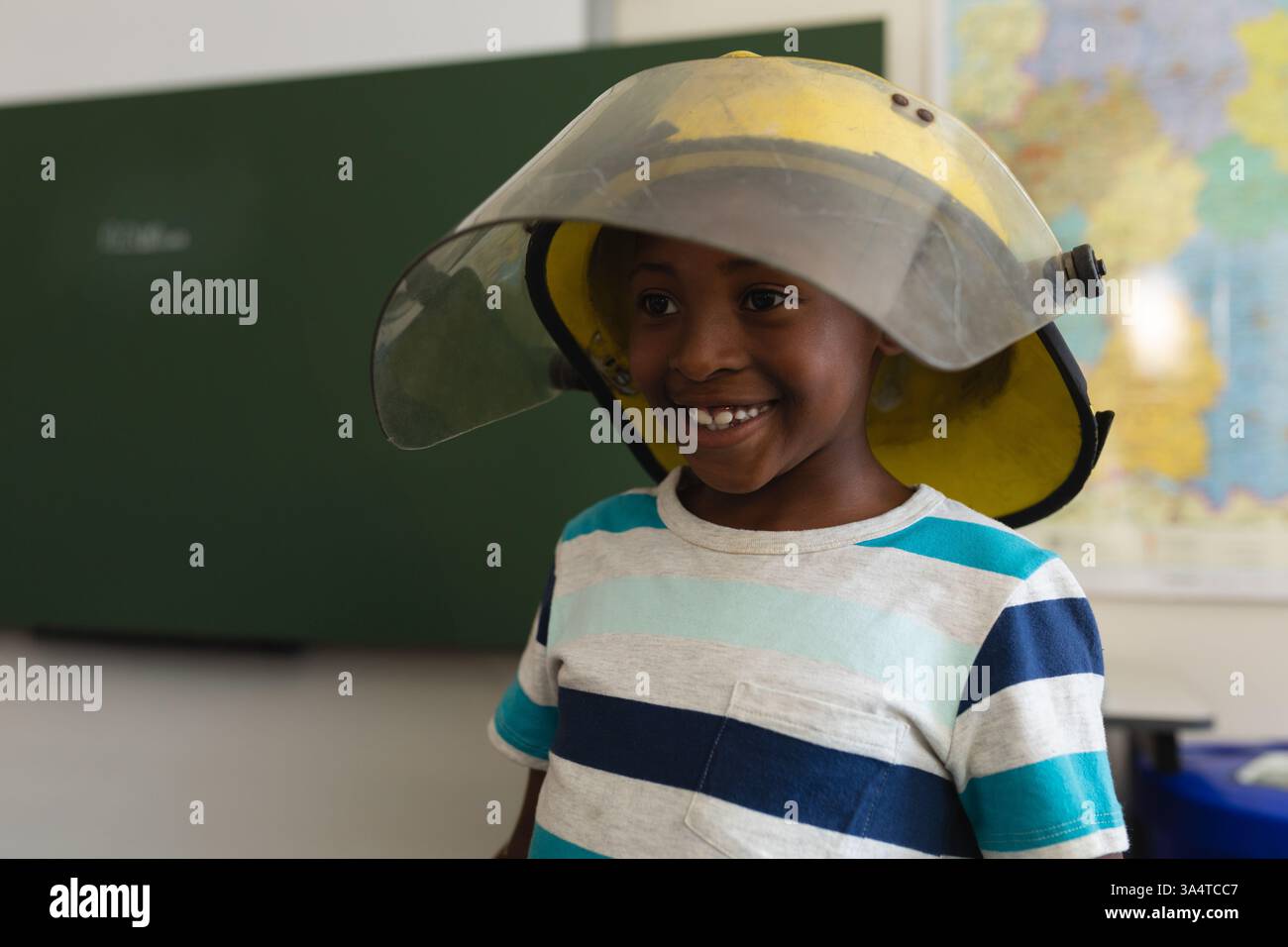 Smiling boy wearing firefighter helmet in classroom, enjoying school ...