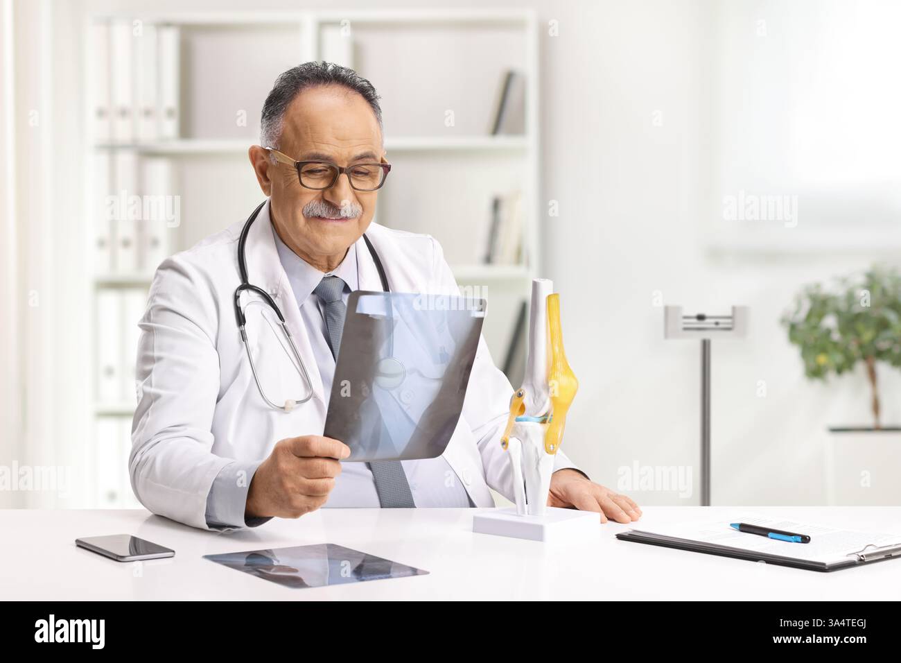 Doctor sitting behind a desk and checking an x-ray image Stock Photo ...