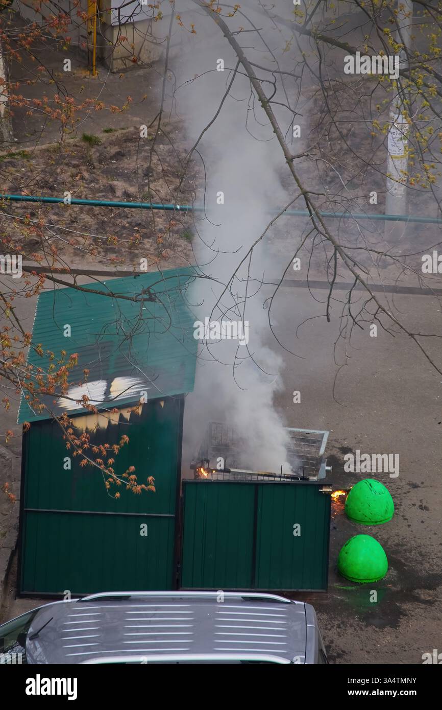 A green metal dumpster shed emitting heavy smoke, indicating a fire ...