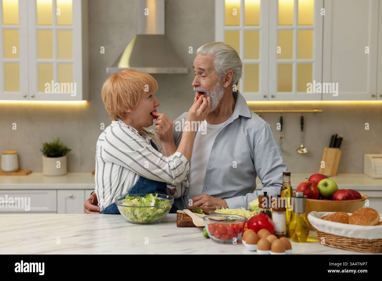 Senior couple feeding each other while cooking in kitchen Stock Photo - Alamy