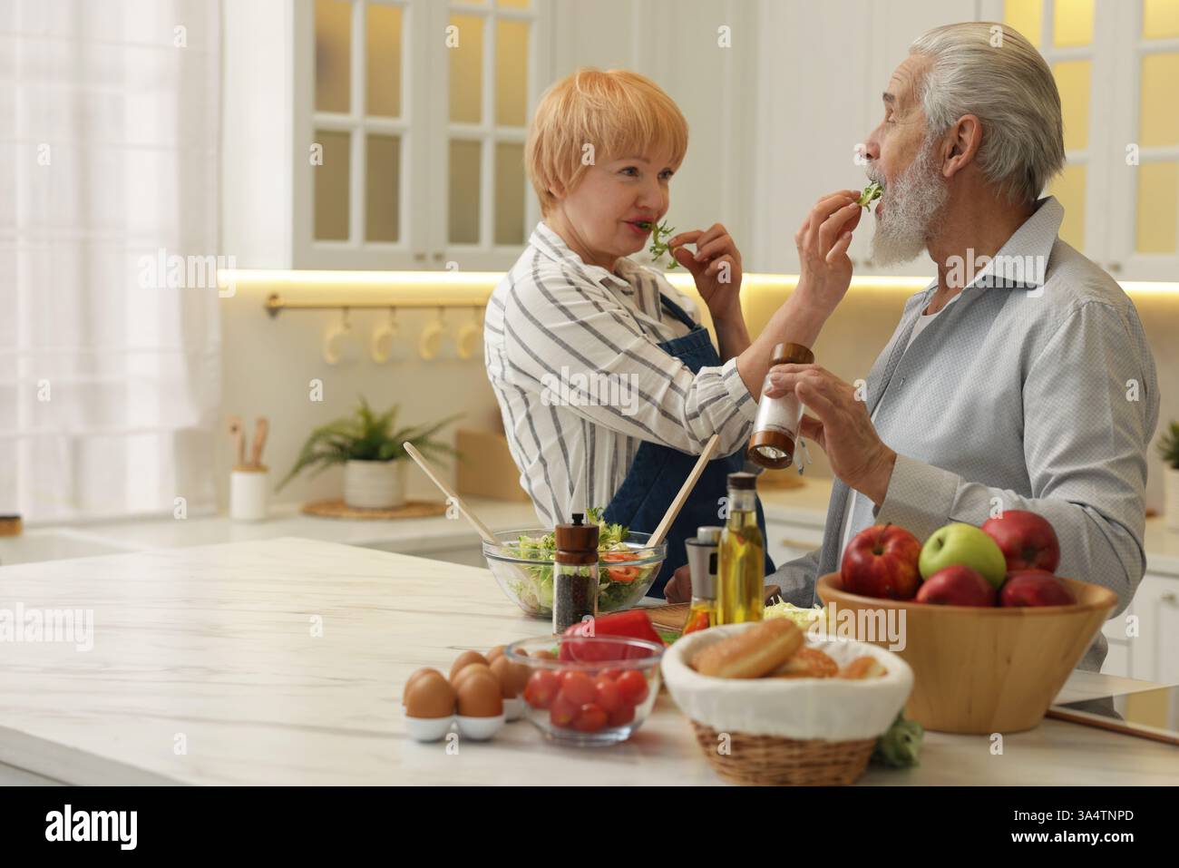 Senior couple feeding each other while cooking in kitchen Stock Photo ...