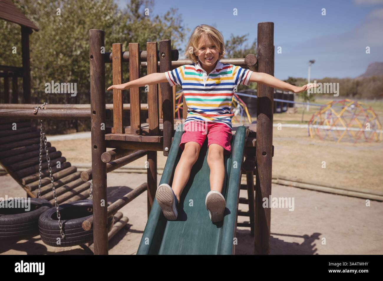 Child sliding down playground slide outdoors, arms outstretched ...
