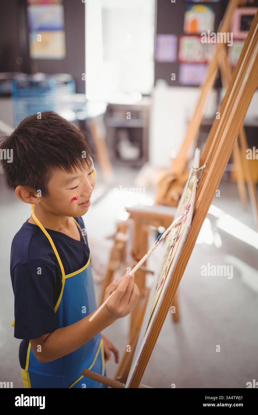 Asian boy painting on easel in art class, enjoying creative activity at ...