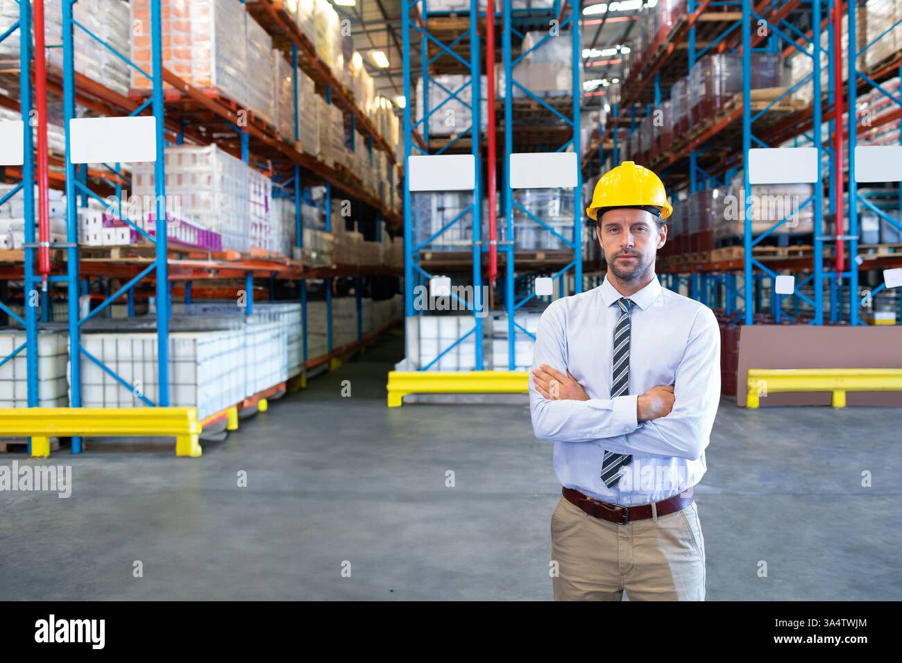 Confident warehouse manager wearing hard hat standing among shelves and ...