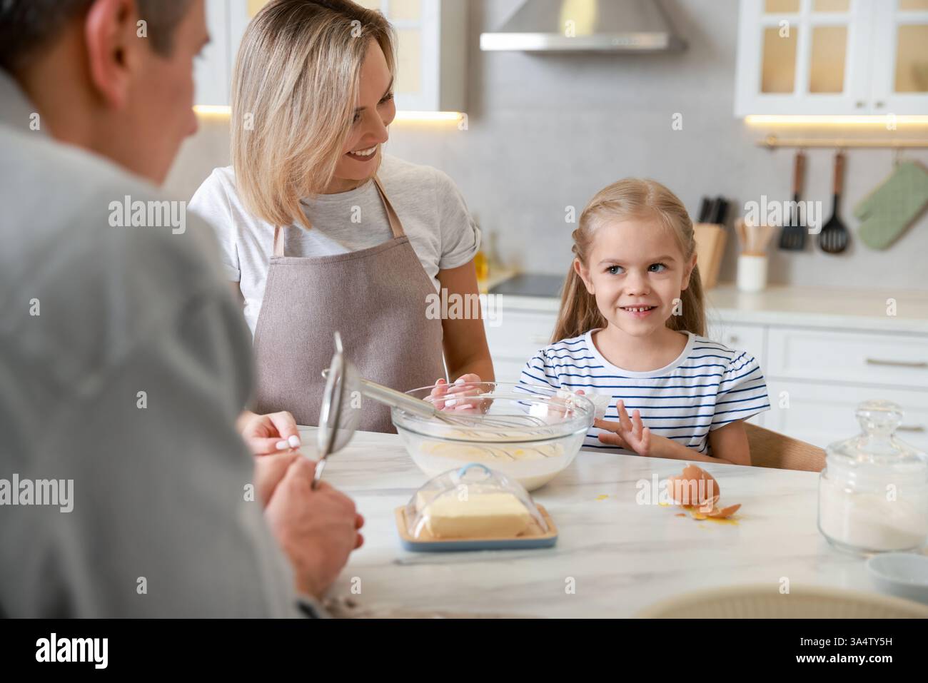 Happy parents and their daughter making dough at white marble table in ...