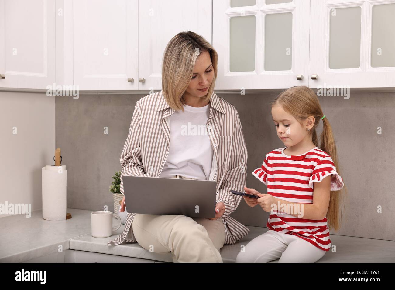 Single mother working with laptop and her daughter in kitchen Stock ...