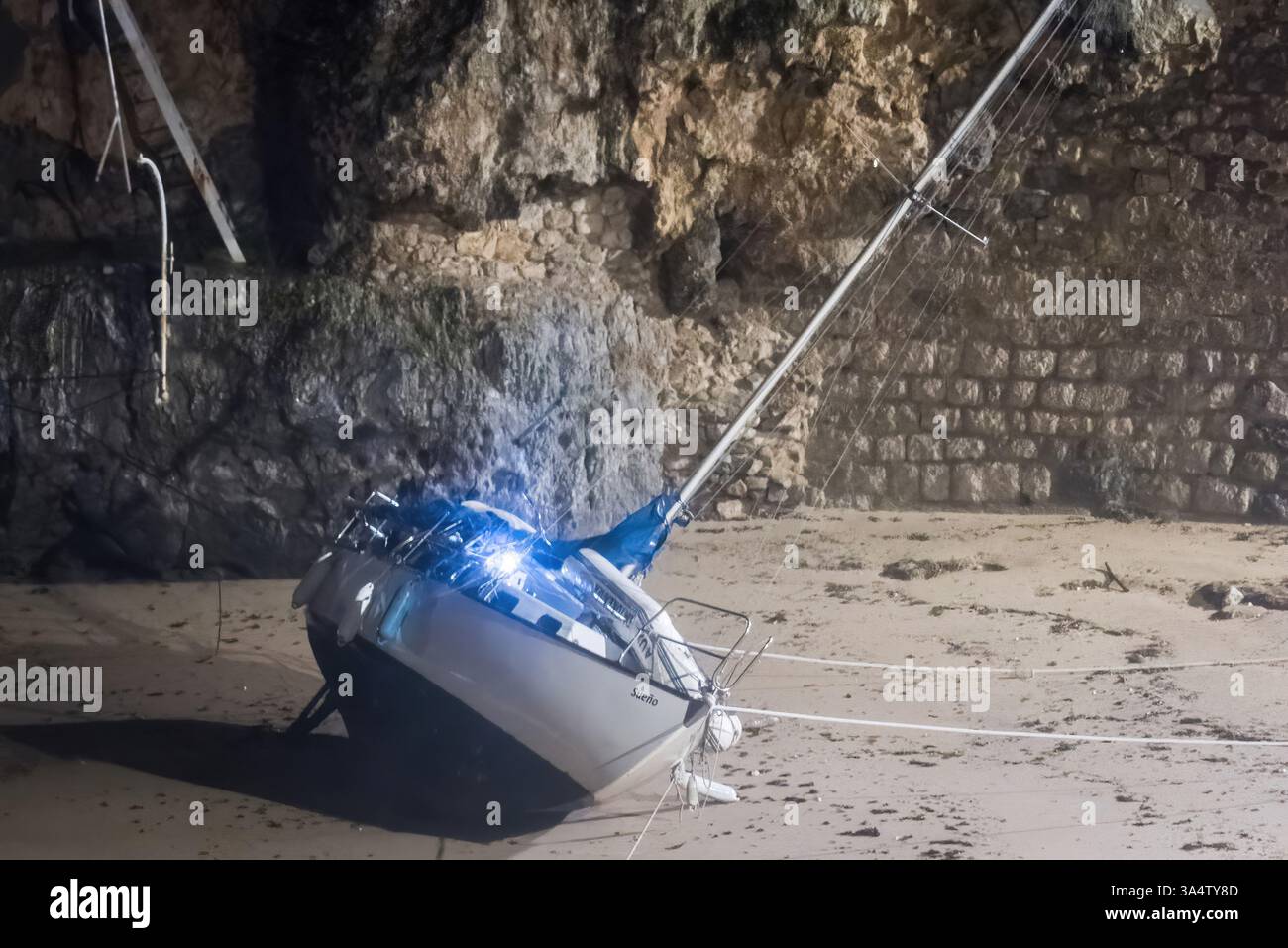 Sailboat stranded on shore at night with solar panels and ocean waves ...