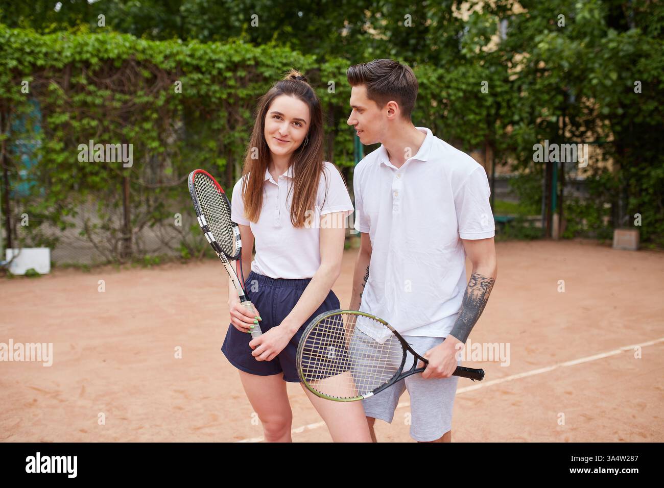 A man and woman stand back-to-back on a tennis court, both holding ...